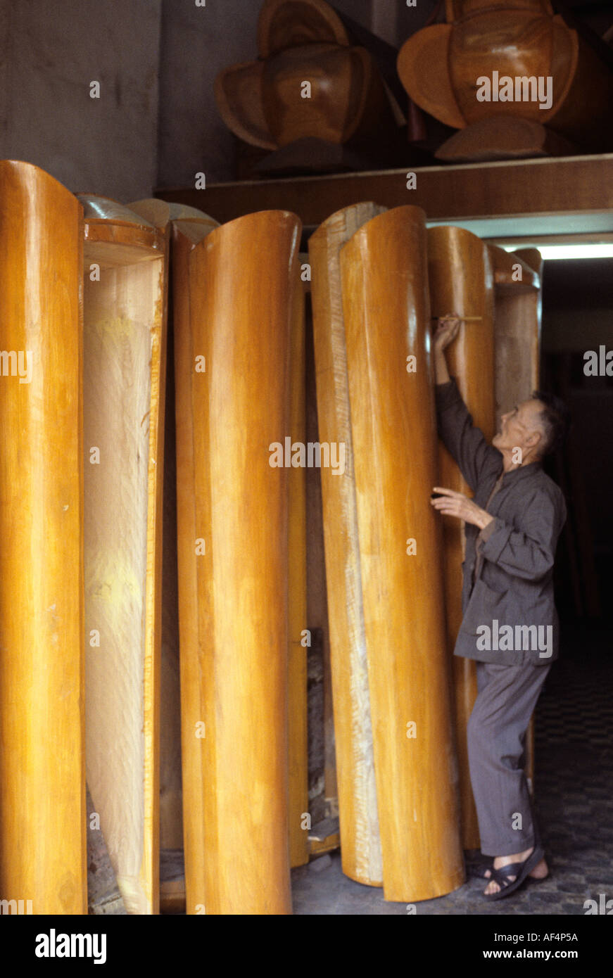 A Chinese man puts finishing touches to round coloured coffins stacked ...