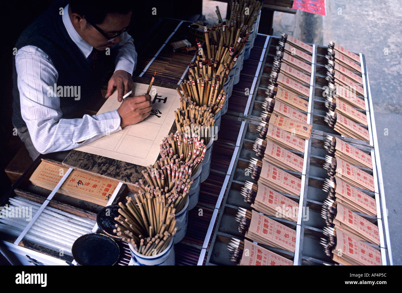 A Chinese man writing characters at a stall selling traditional writing ...