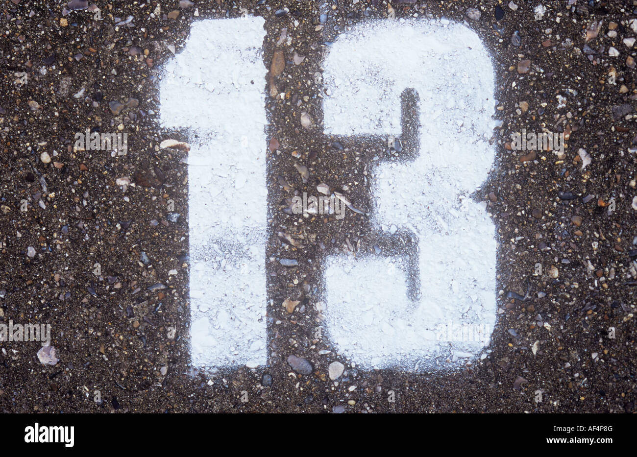 Close up of white painted stencilled number 13 on rough concrete wall ...