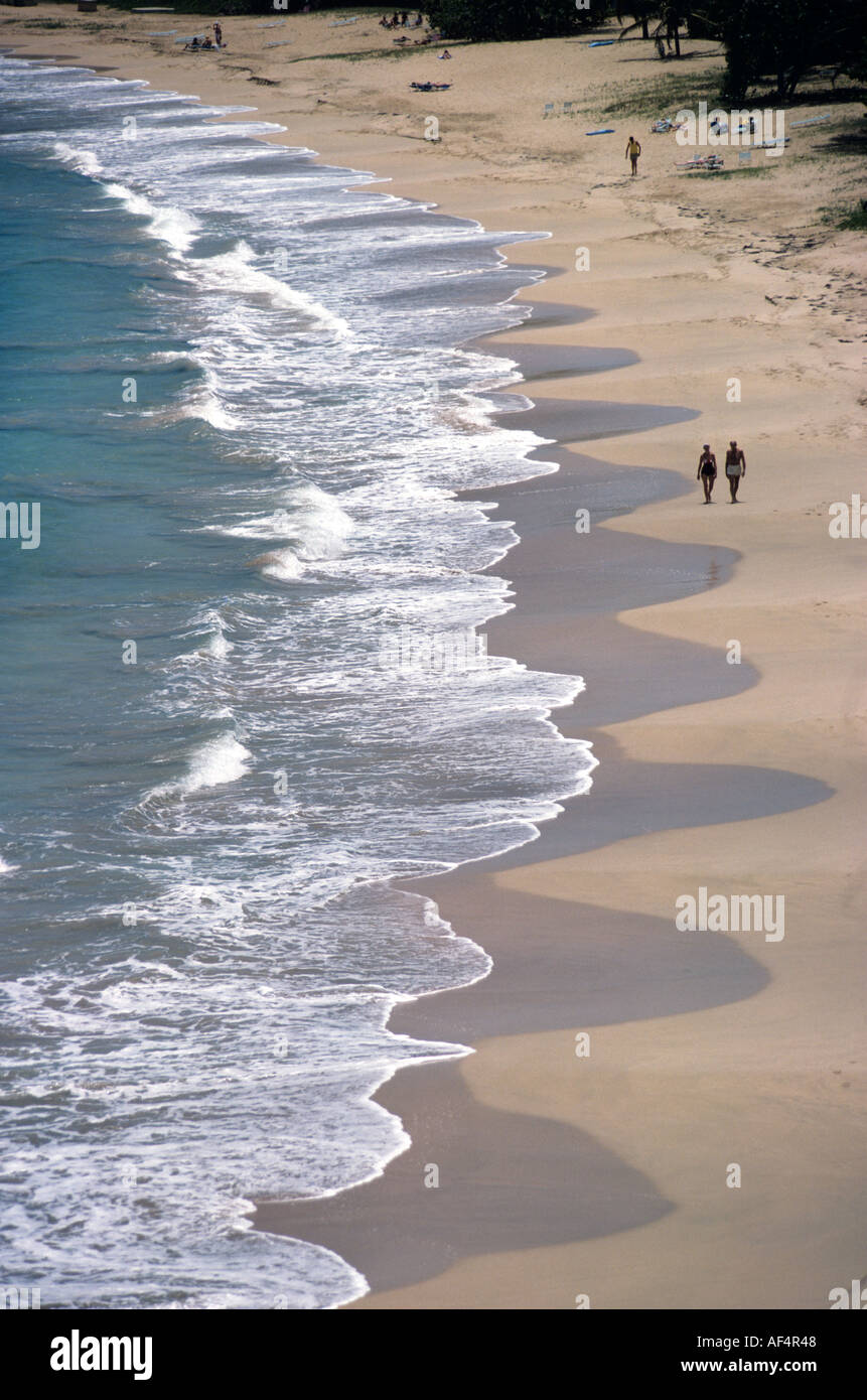 Small waves breaking as surf on curved sand beach with couple walking ...