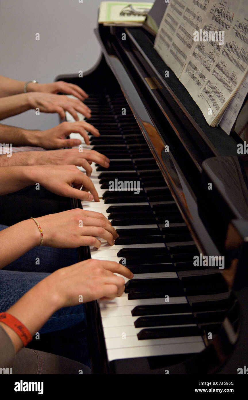Four people play on the same piano. A partition open on the music stand ...