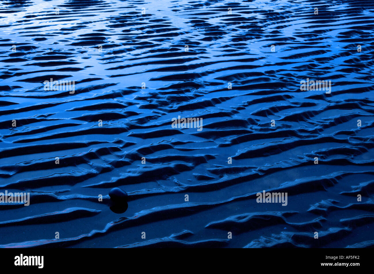 single pebble on beach cold blue colour ripples in sand water seaside ...