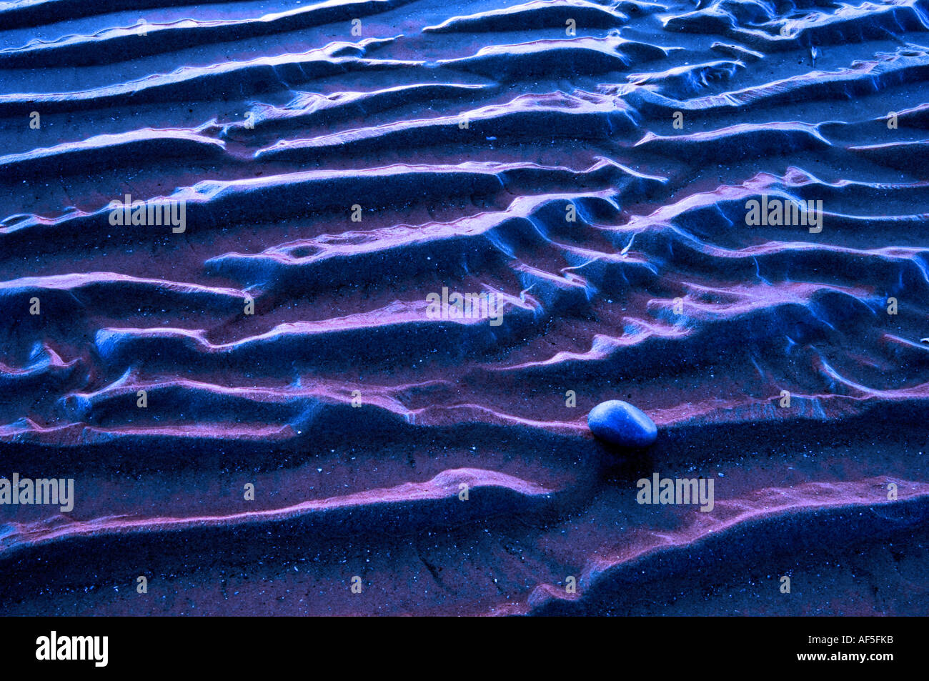 single pebble on beach cold blue colour ripples in sand water seaside ...
