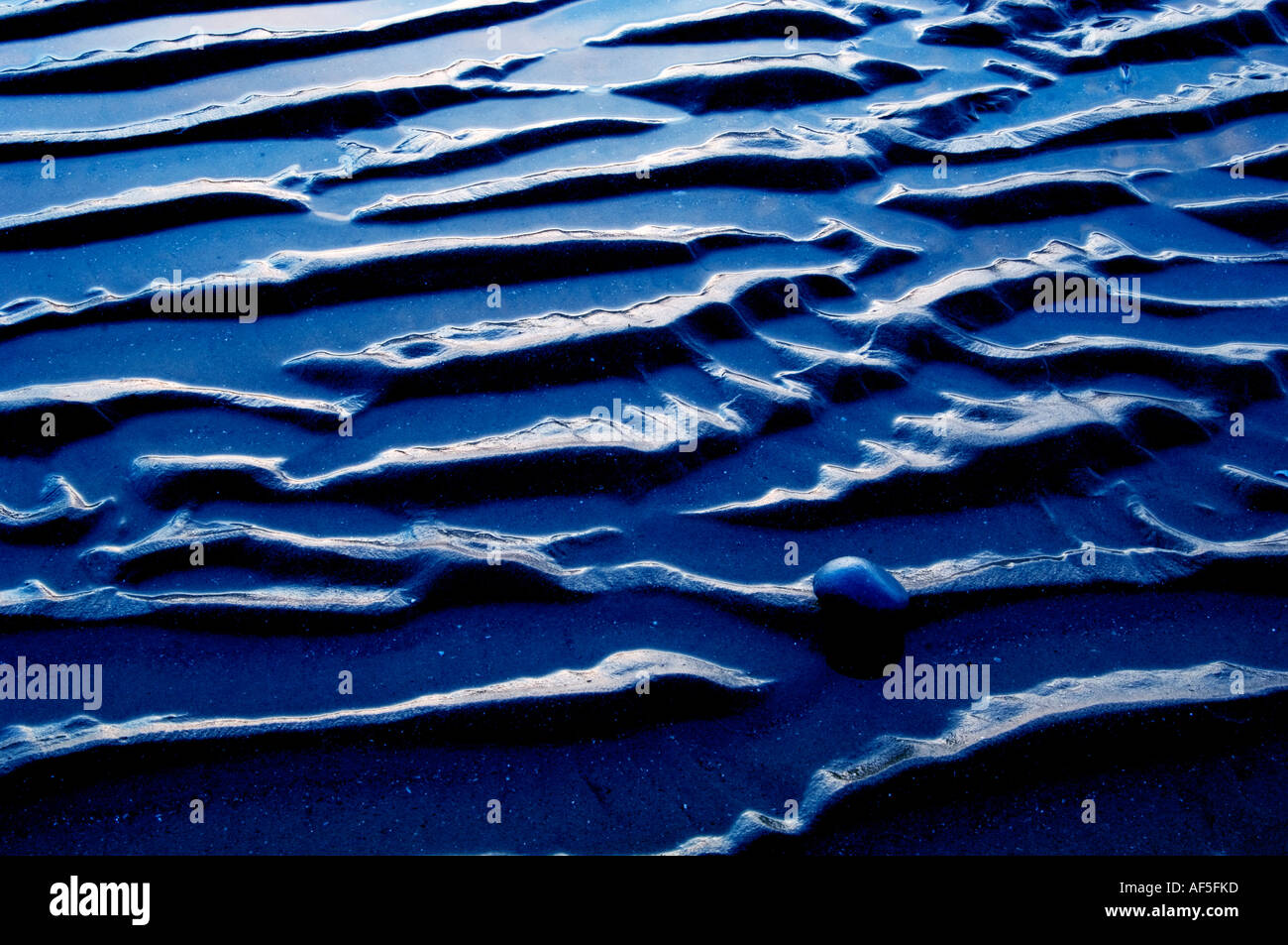 single pebble on beach cold blue colour ripples in sand water seaside ...