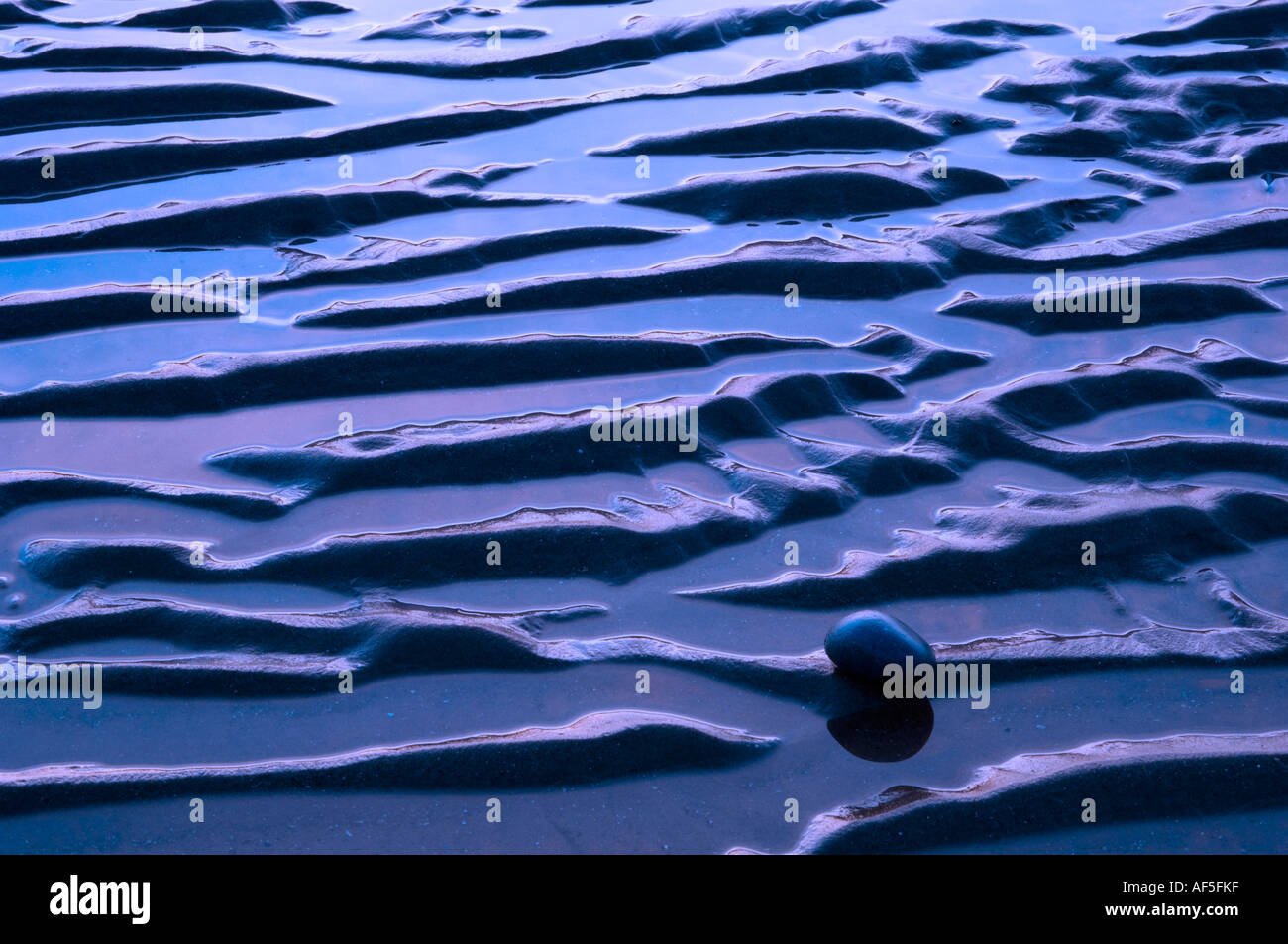 single pebble on beach cold blue colour ripples in sand water seaside ...