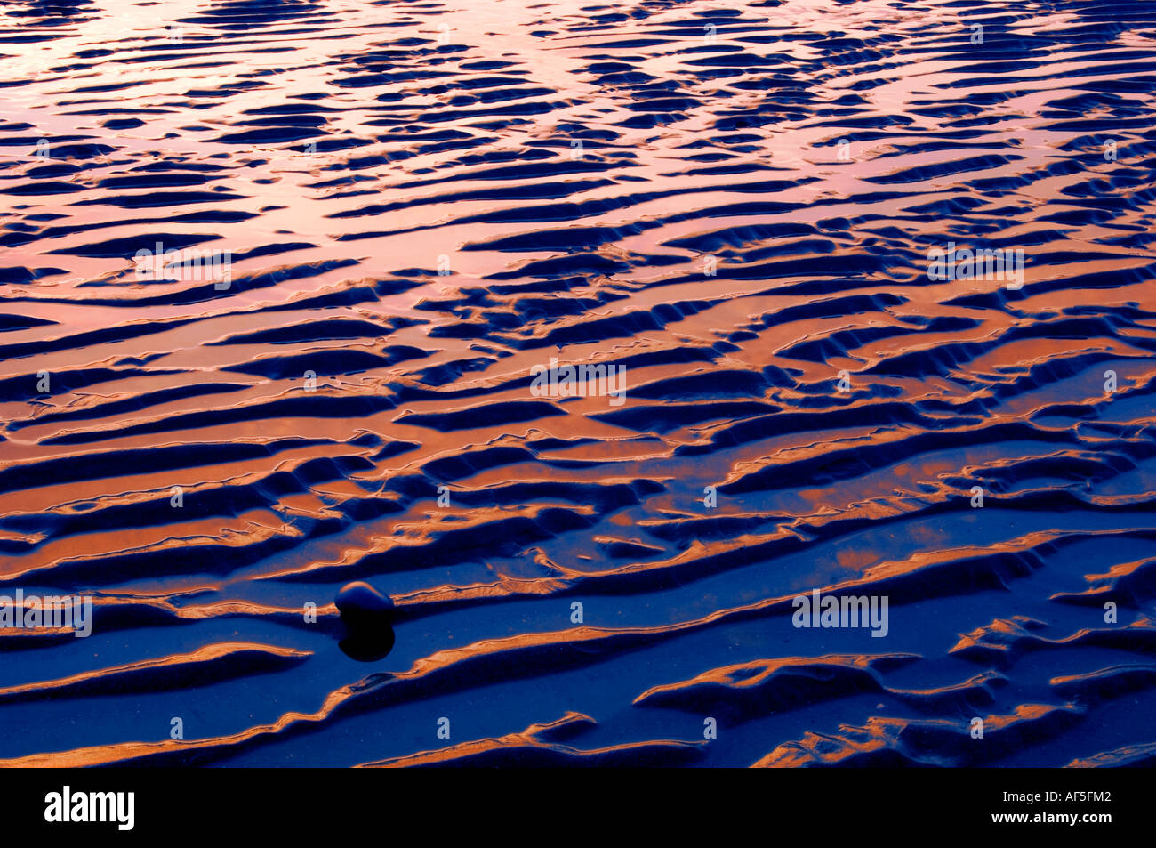 single pebble on beach cold blue colour ripples in sand water seaside ...