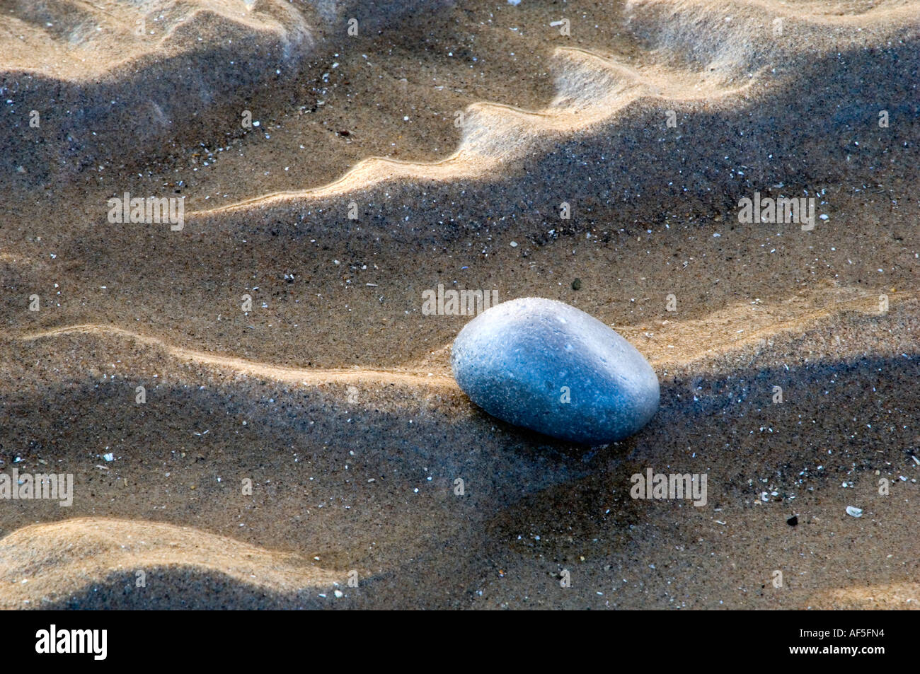 single pebble on beach cold blue colour ripples in sand water seaside ...
