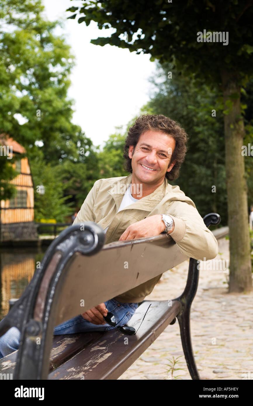 Confident man smiling sitting on a bench outdoor Stock Photo - Alamy