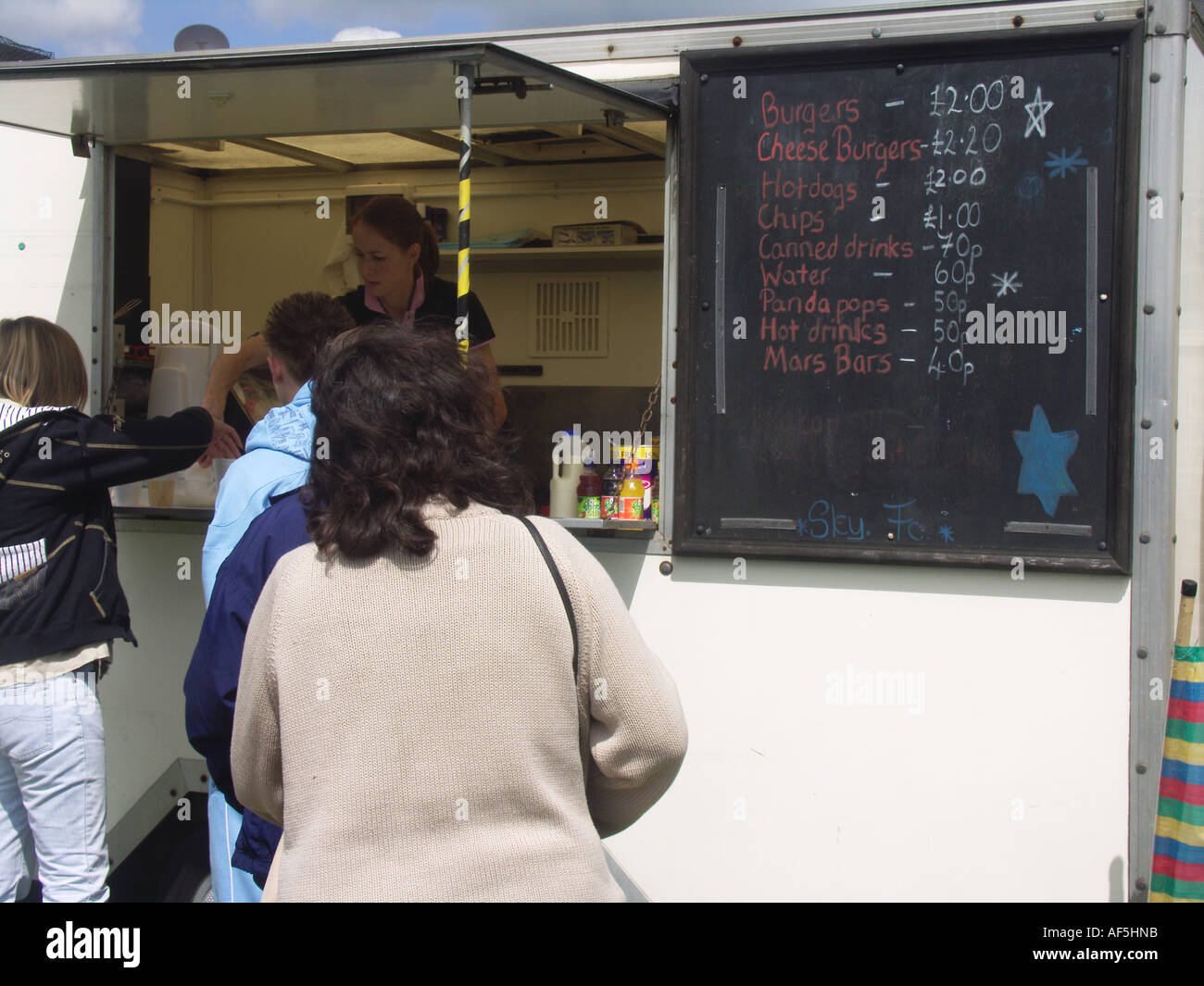 Queue of people at a burger mobile fast food stall with woman serving ...