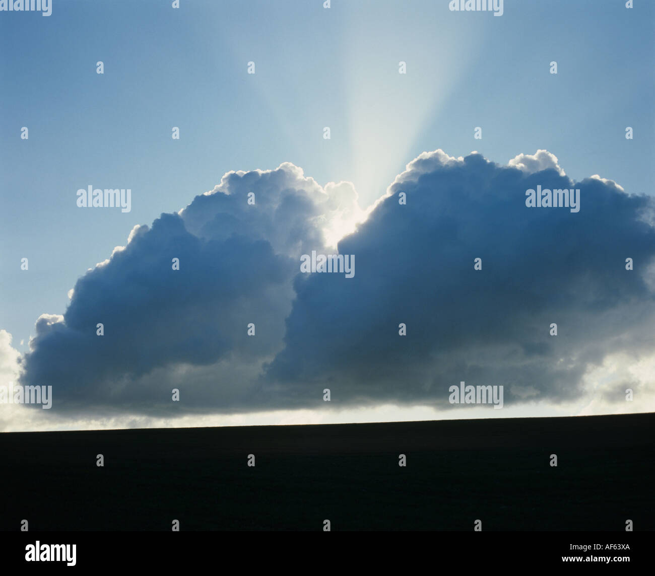 Sun behind cumulus clouds with shaft of sunlight against blue sky Stock ...