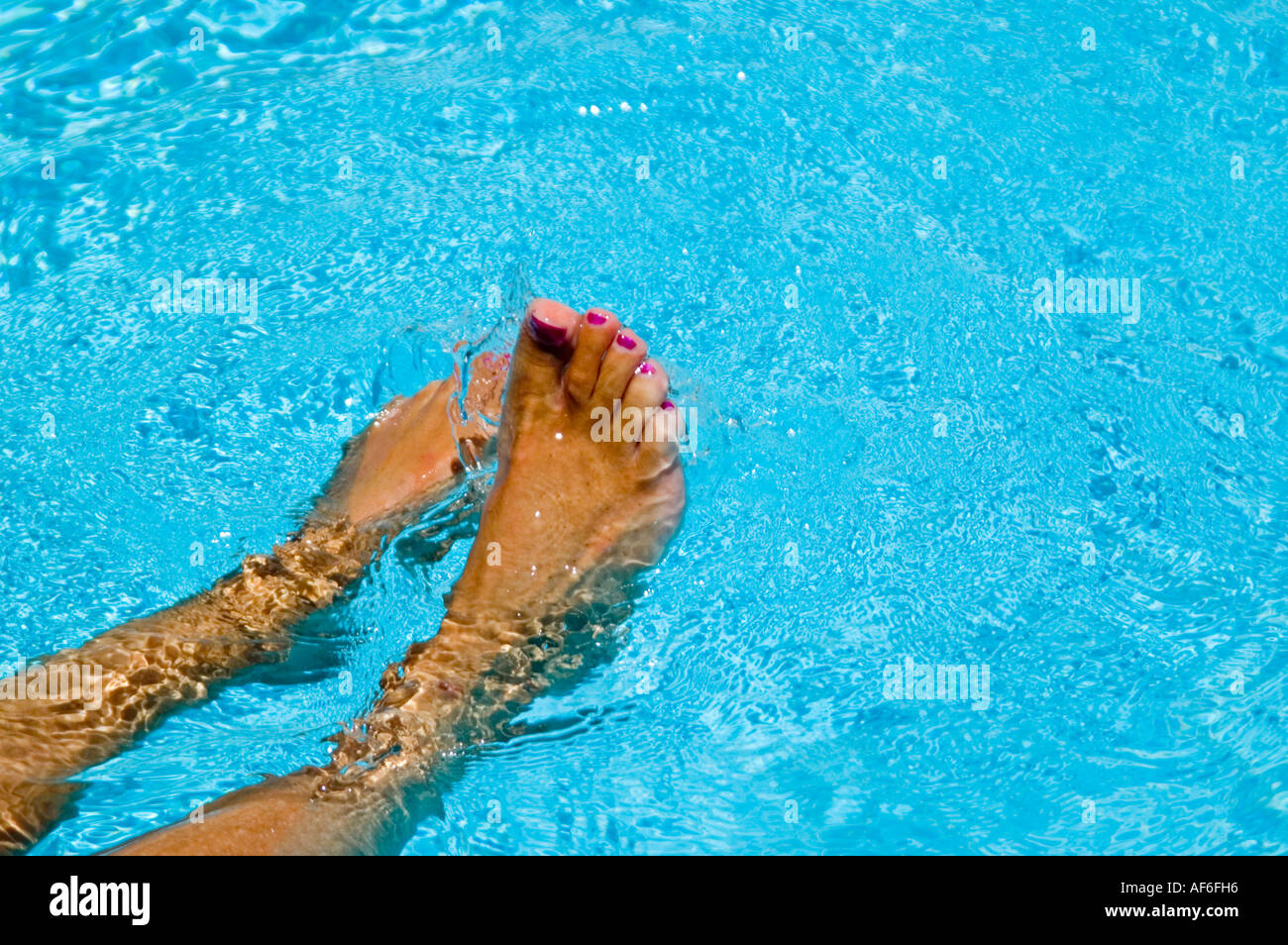 Horizontal close up of tanned wet feet with painted toenails splashing ...