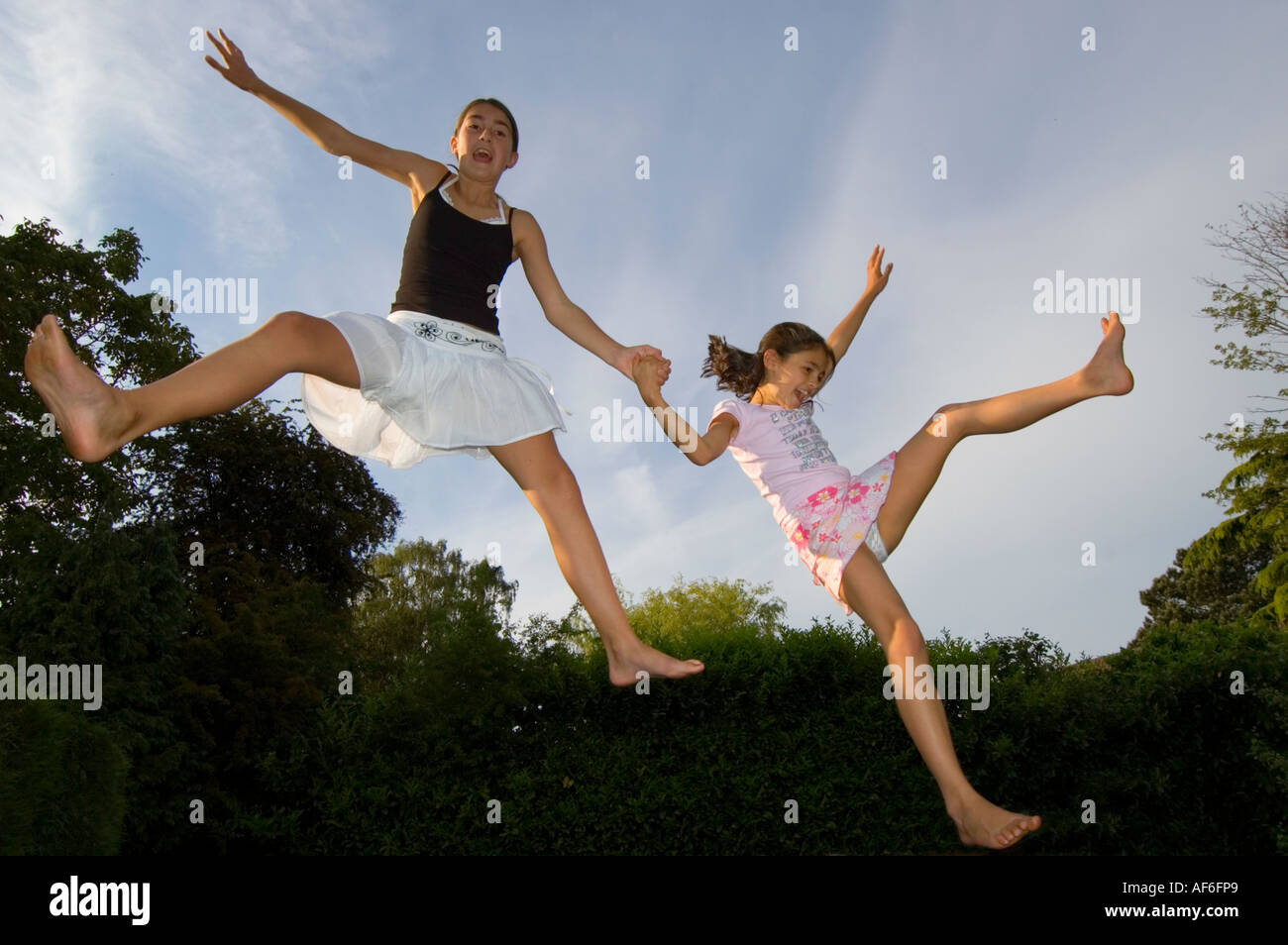 Horizontal portrait of two girls in mid air having fun bouncing on a ...