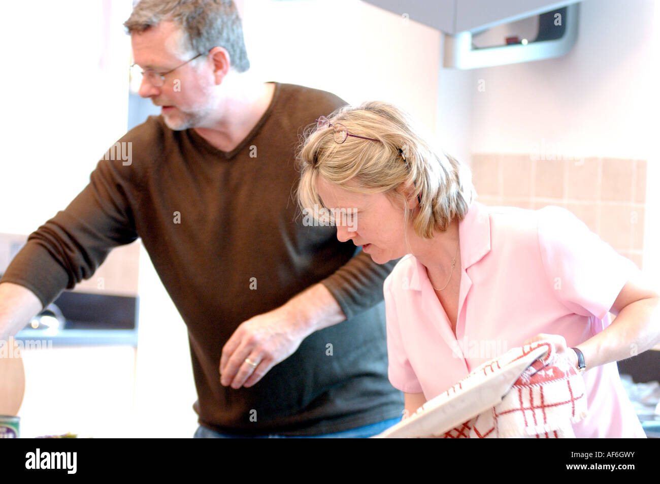 British man and woman husband and wife couple in kitchen cooking with a ...