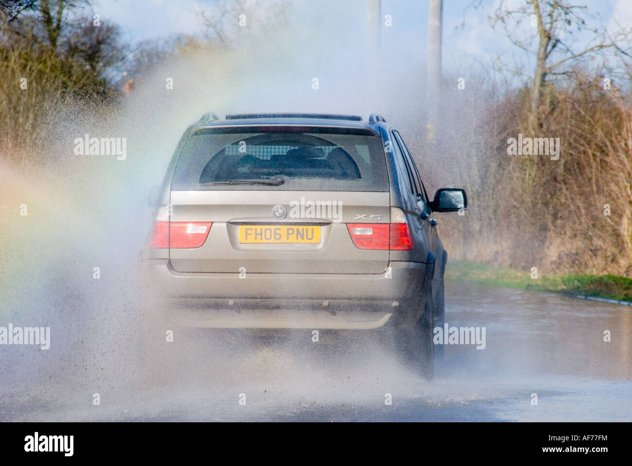 BMW X5 car driving driving through flood on a rural road in england ...