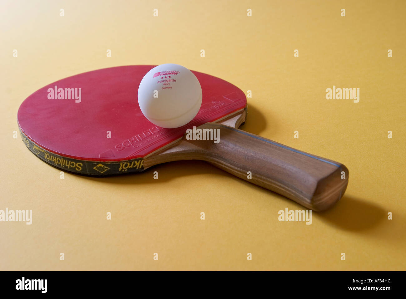 table tennis bat with ping pong ball resting on it on a yellow ...