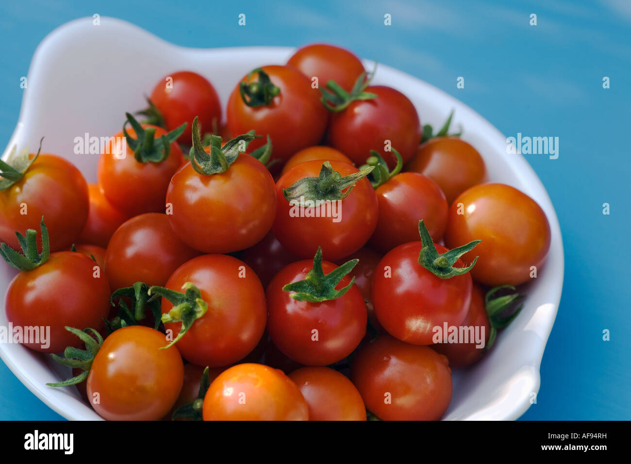 Bowl of cherry tomatoes on a blue table Stock Photo - Alamy