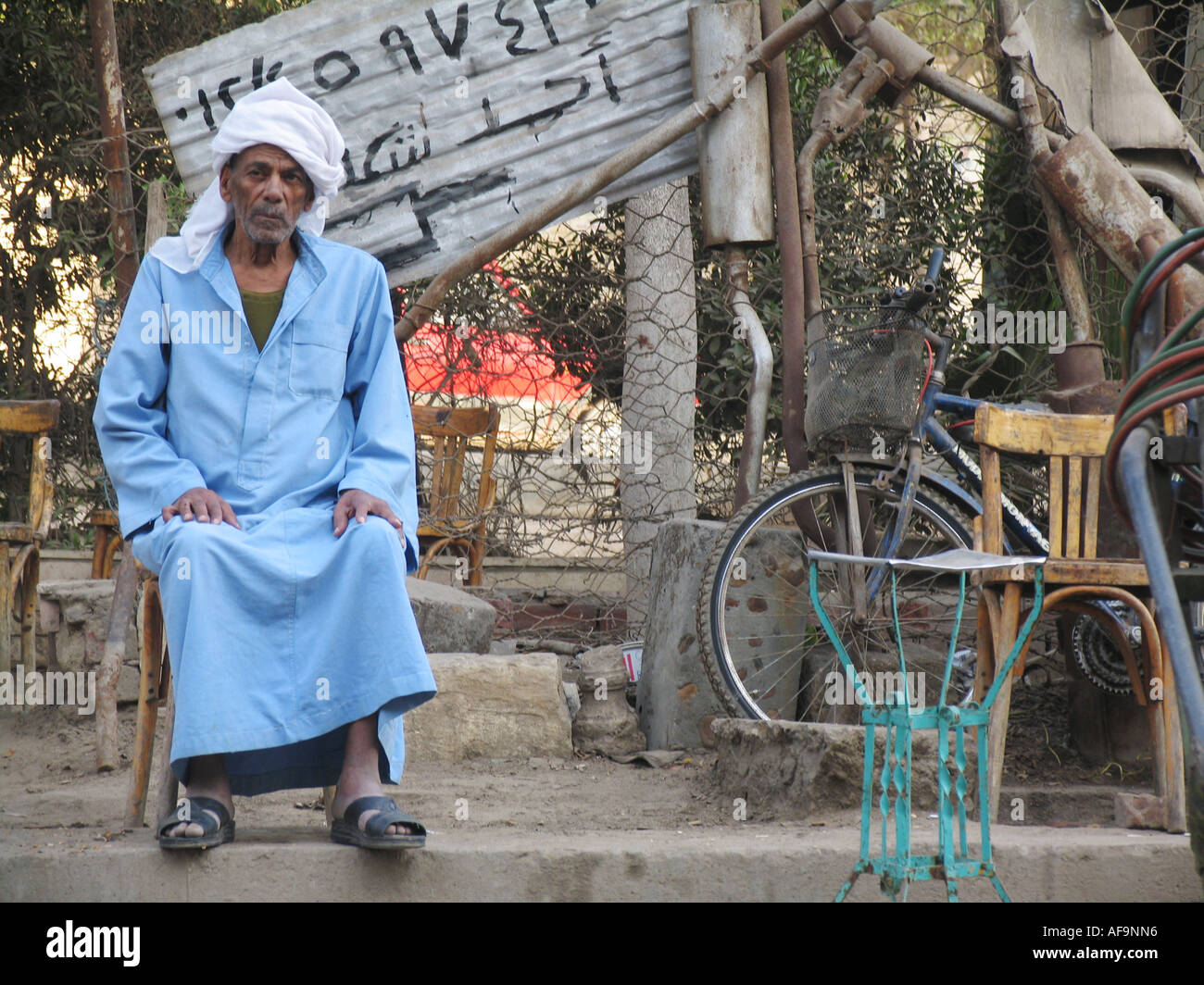 Man on chair with headgear (turban) next to junk in poor area of Cairo ...