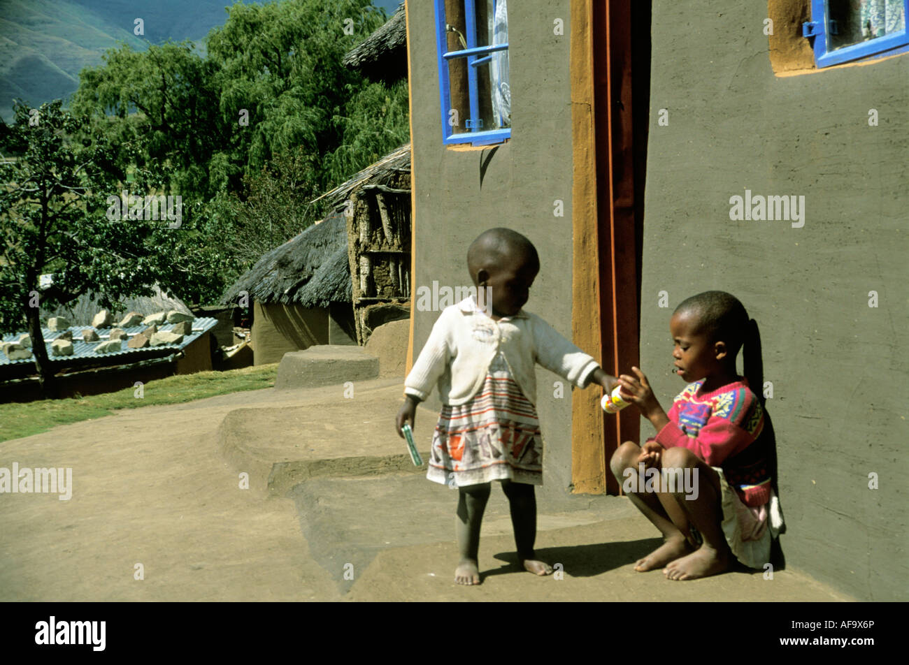 Two small black children, one sitting and one standing outside their ...