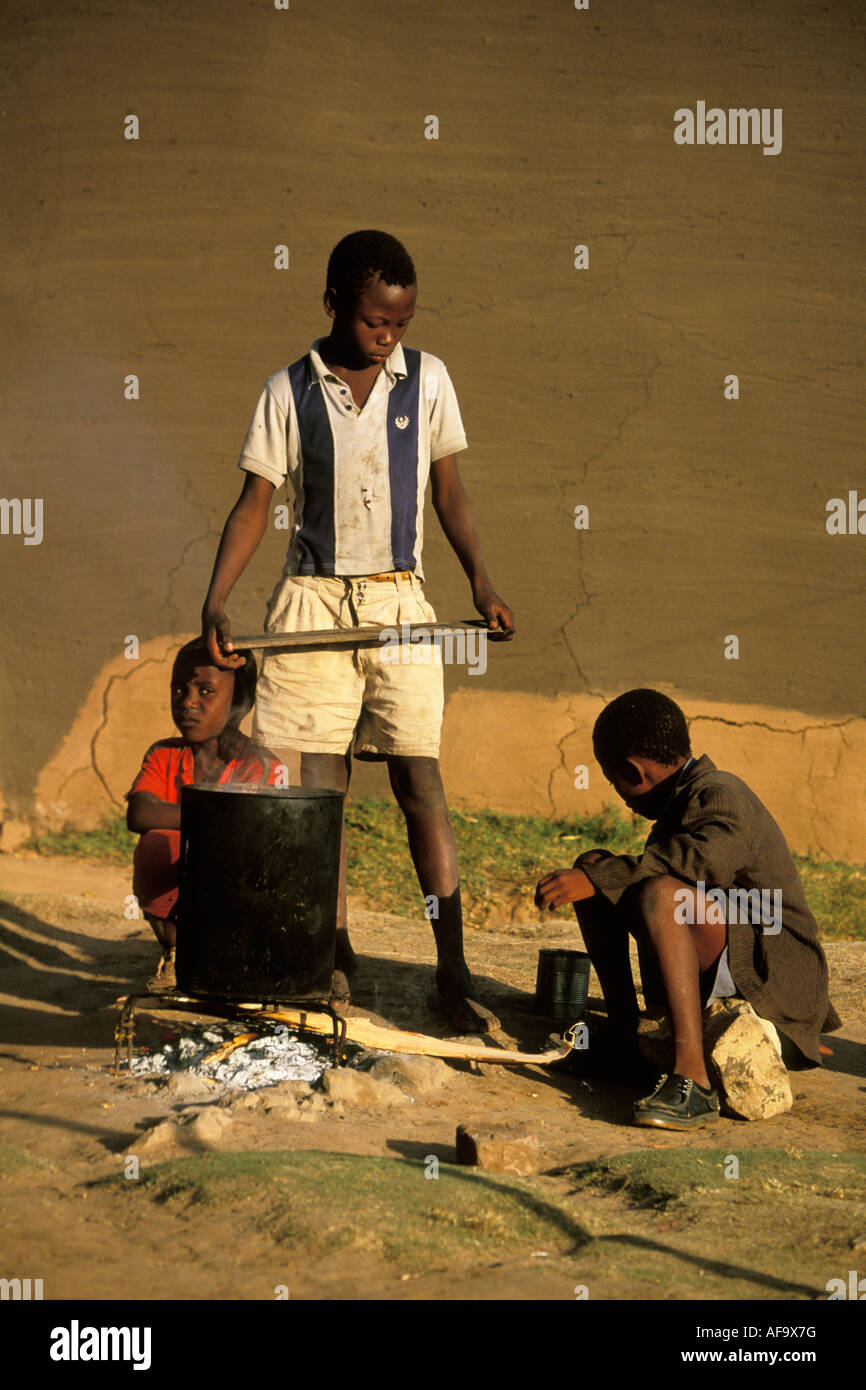 Group of three young black youths tending a large black cooking pot ...