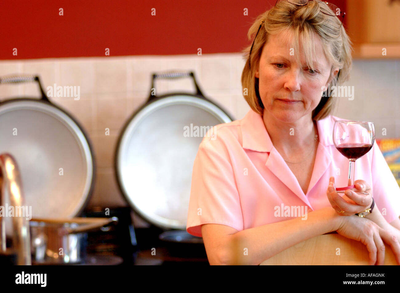 British middle aged woman in kitchen relaxing drinking wine at the ...