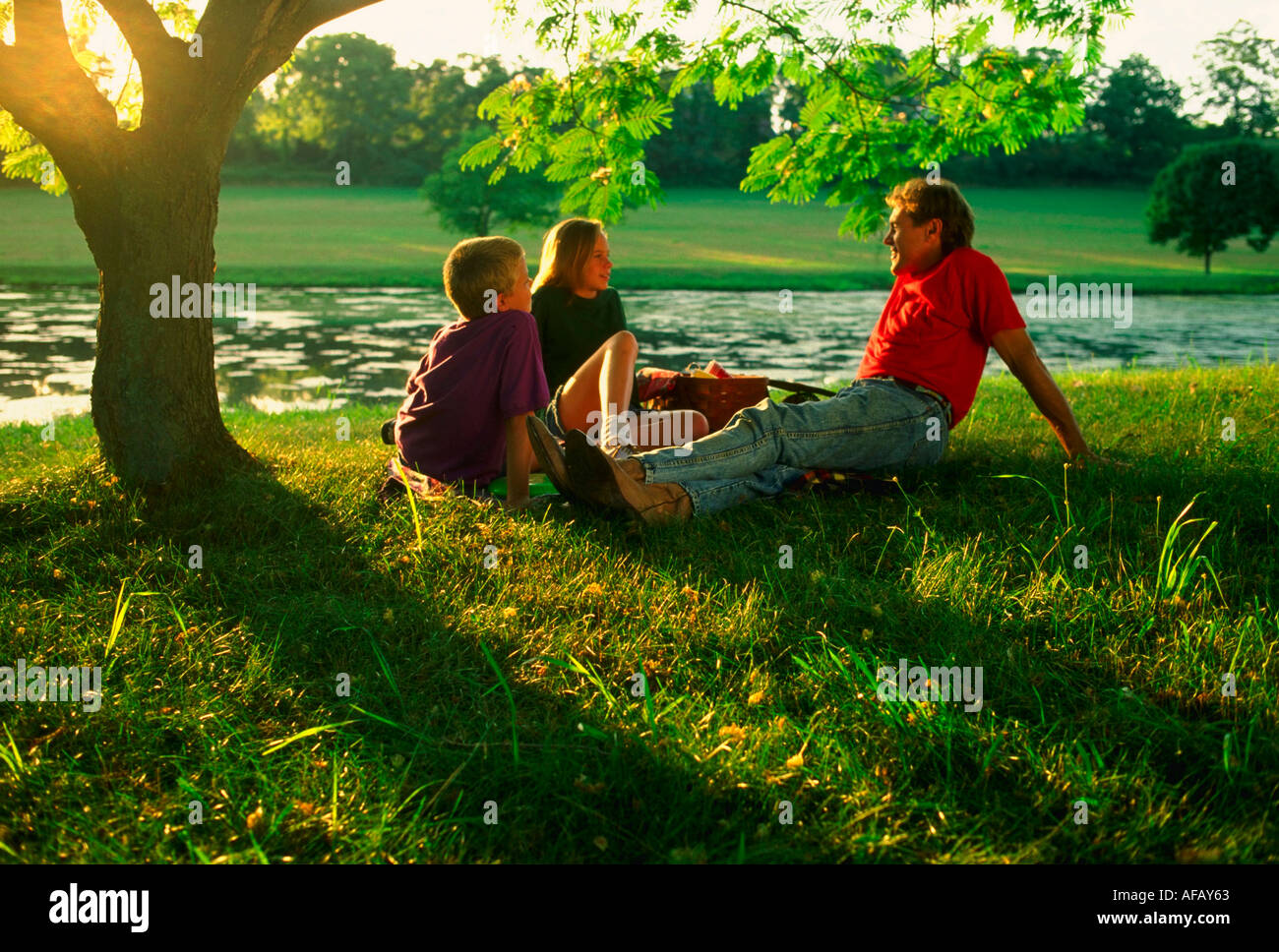 Dad son daughter relax under tree after picnic at farm pond MR Stock ...