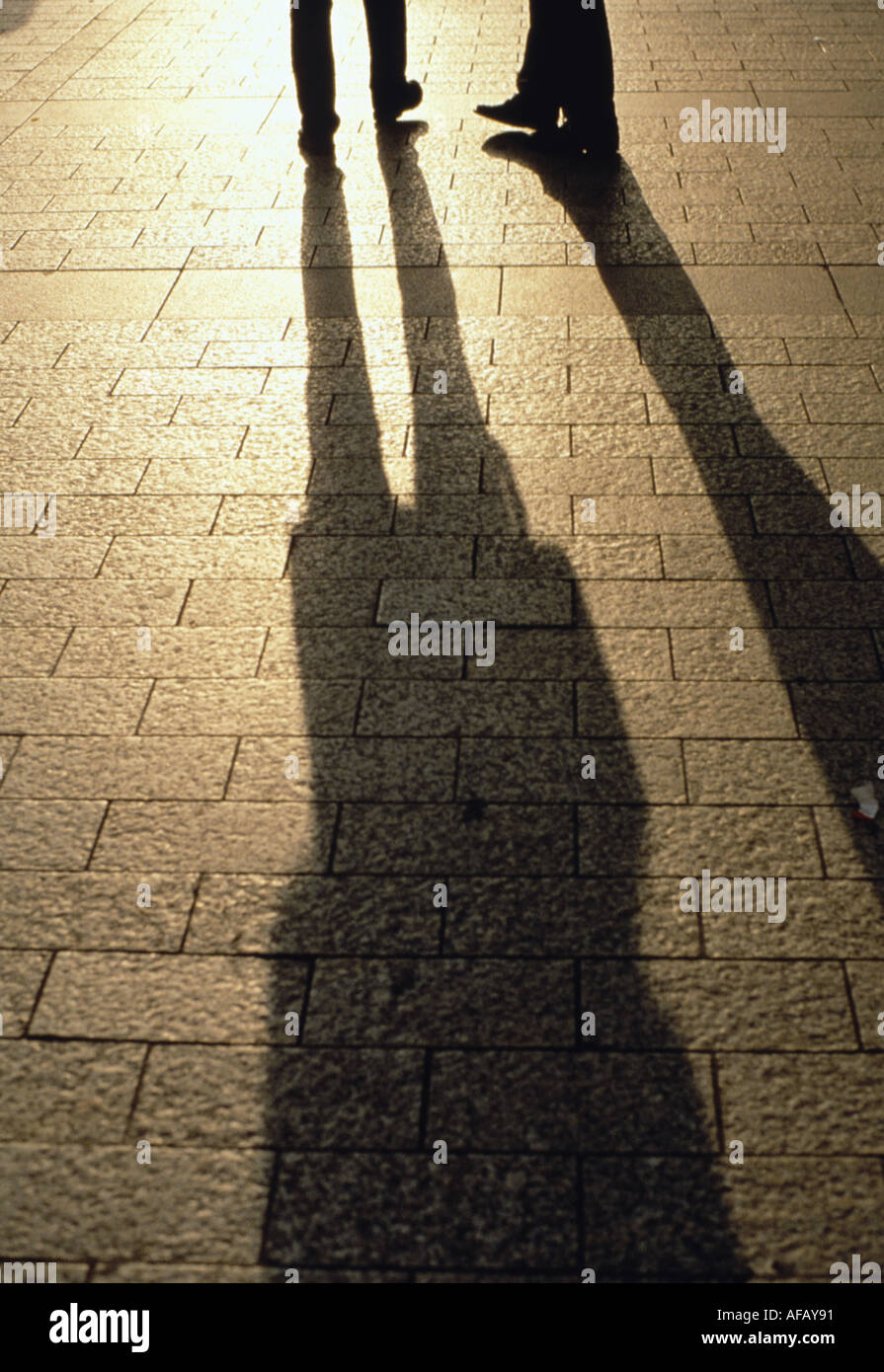 Long shadows cast by two people standing on the sidewalk talking in the ...