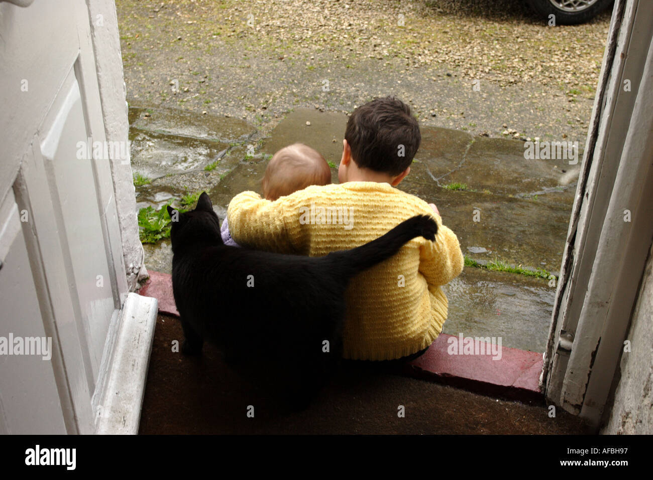 Brother and sister cuddle on the doorstep raining outside Stock Photo ...