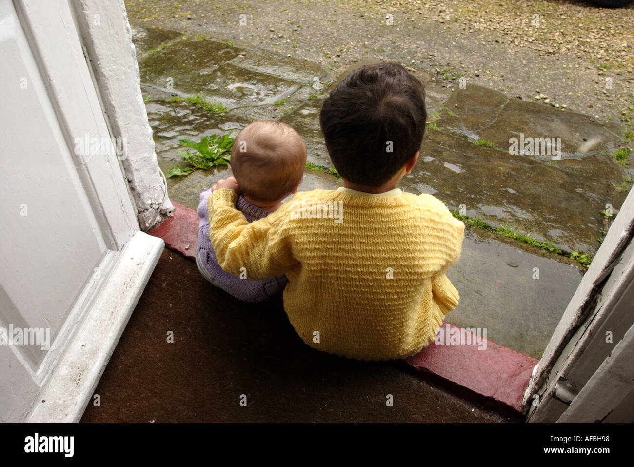 Brother and sister cuddle on the doorstep raining outside Stock Photo ...