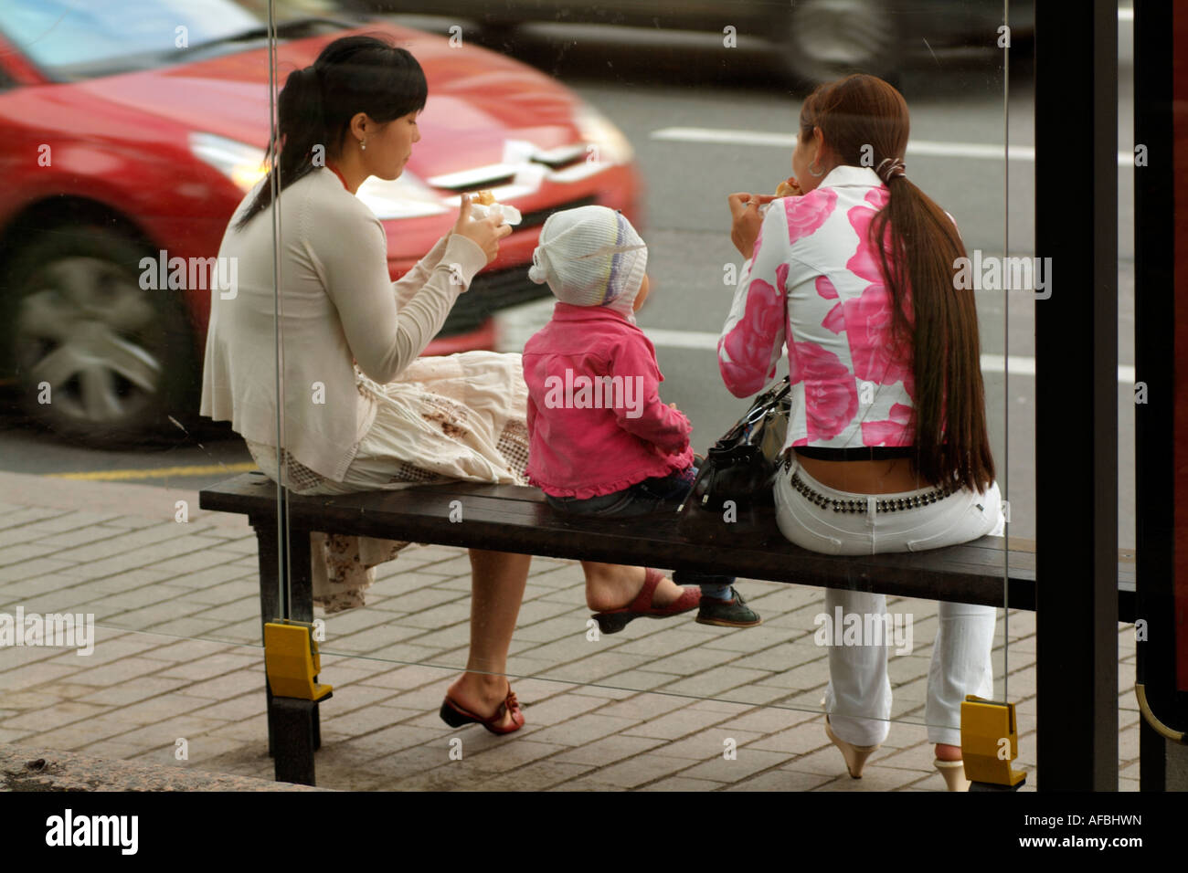 Women with a child eating ice cream sit on a bus shelter seat St ...
