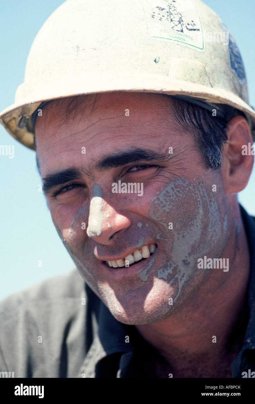 A roughneck oil worker covered in mud wearing a hard hat at a wildcat ...