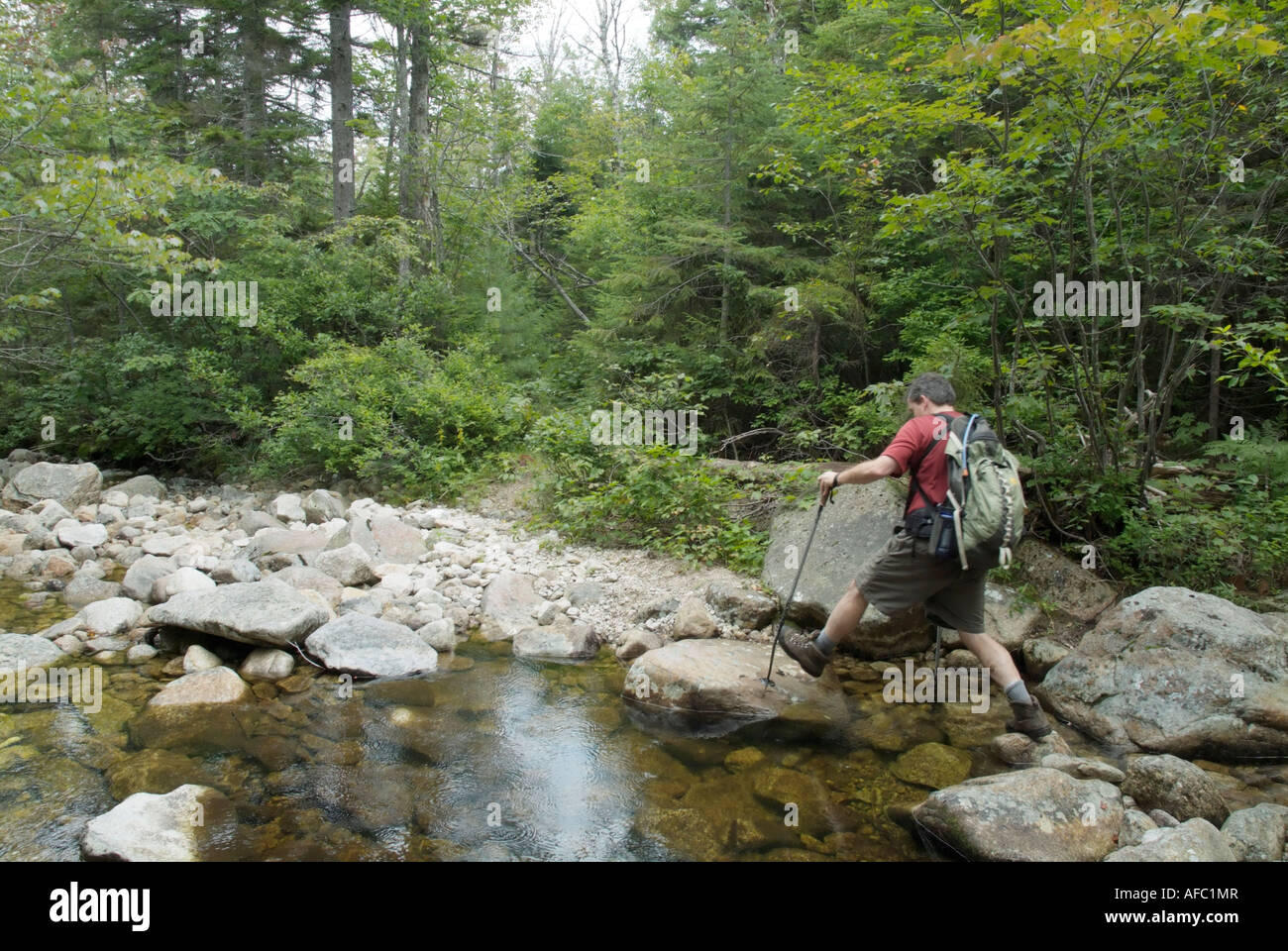 A hiker crosses Sawyer River on Hancock Notch Trail during the summer ...