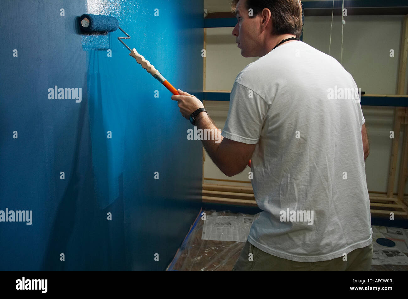 A man using a paint roller to paint a wall blue Stock Photo - Alamy