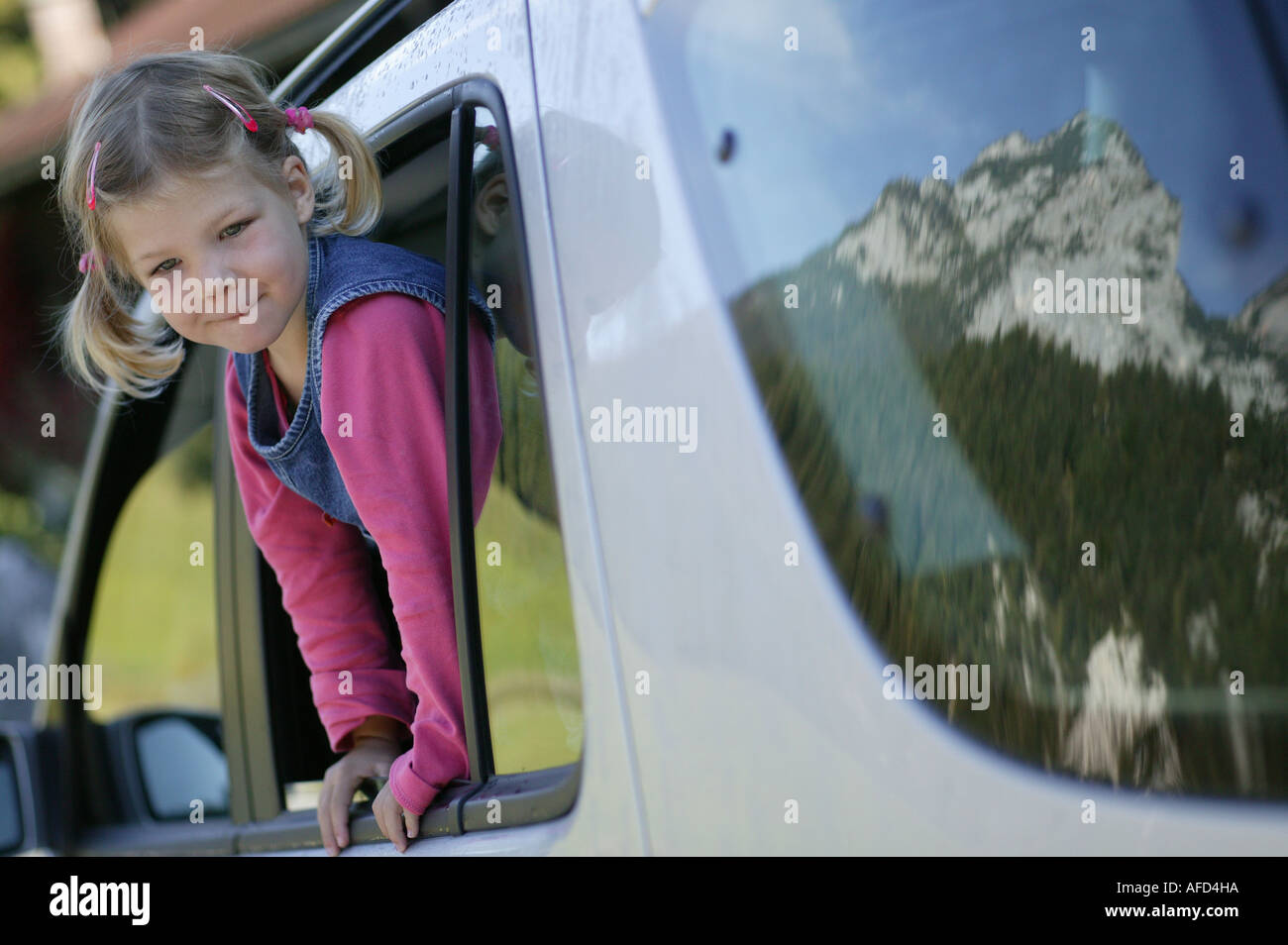 Young girl looking out the car window, reflection of mountains in the ...