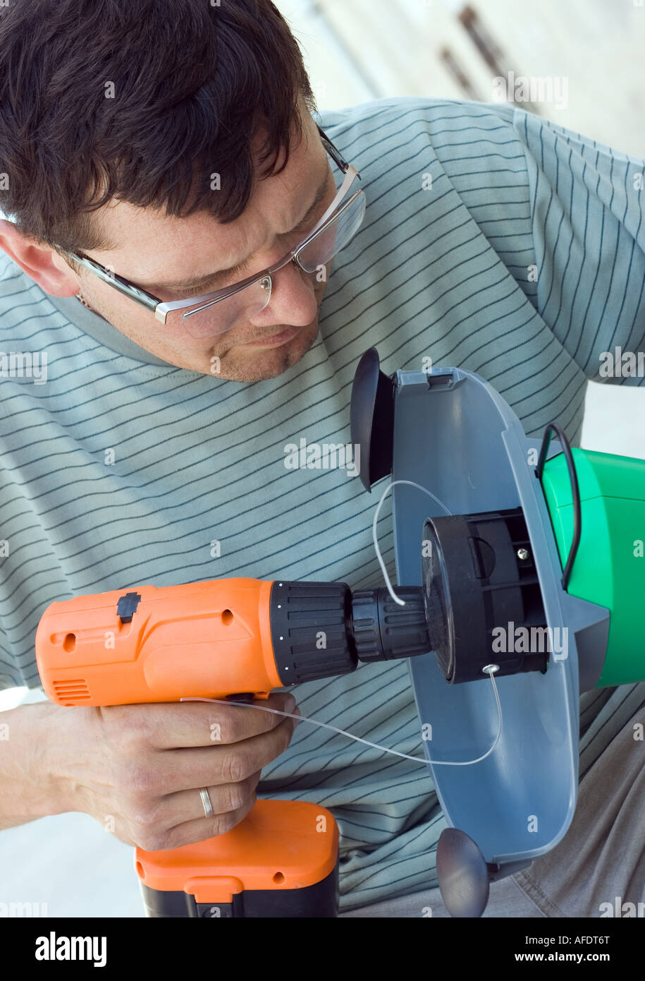 The man, repairs trimmer with an electric screwdriver Stock Photo - Alamy