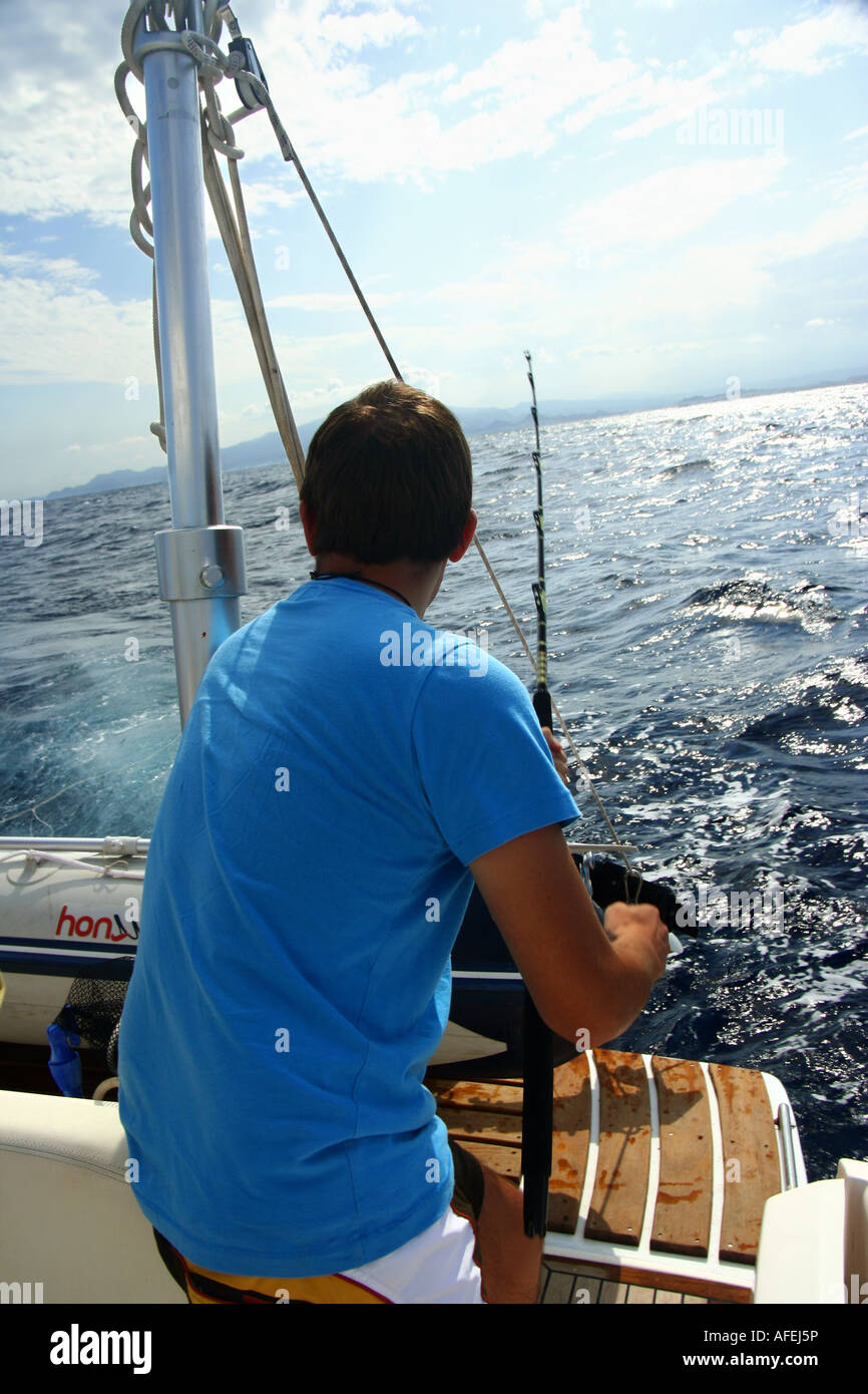 Young man fishing from a ship using a fishing rod Stock Photo - Alamy