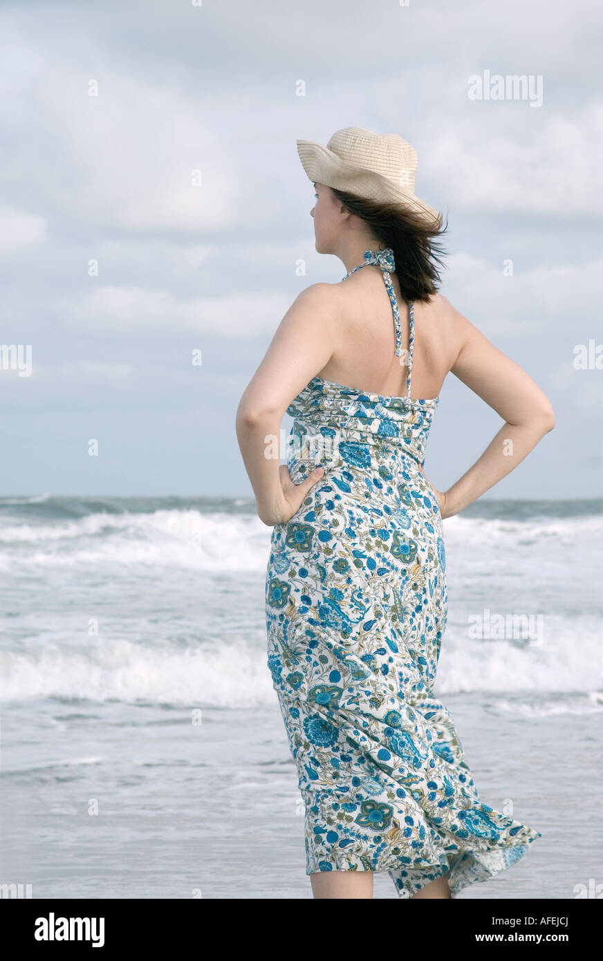 Young woman in blue and white dress standing on the beach hands on hips ...