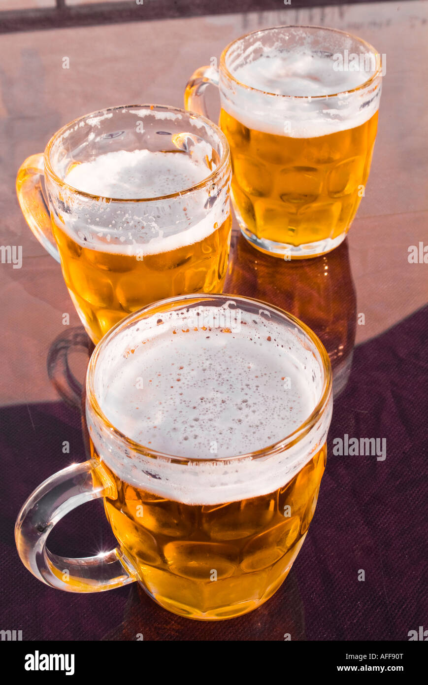 Three glass mugs full of beer sitting on table Stock Photo - Alamy
