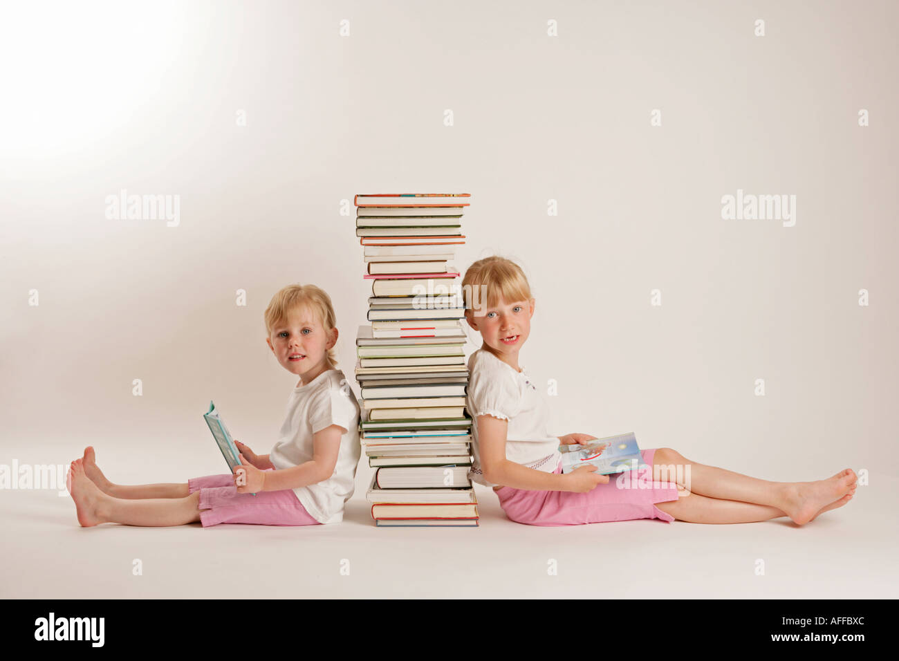 Two girls reading books leaning against a book stack Stock Photo - Alamy