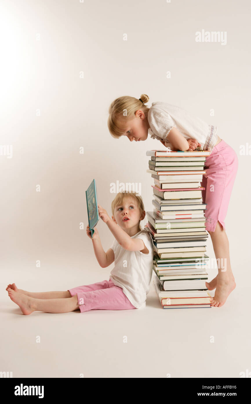 Two girls sitting on a pile of books reading together Stock Photo - Alamy