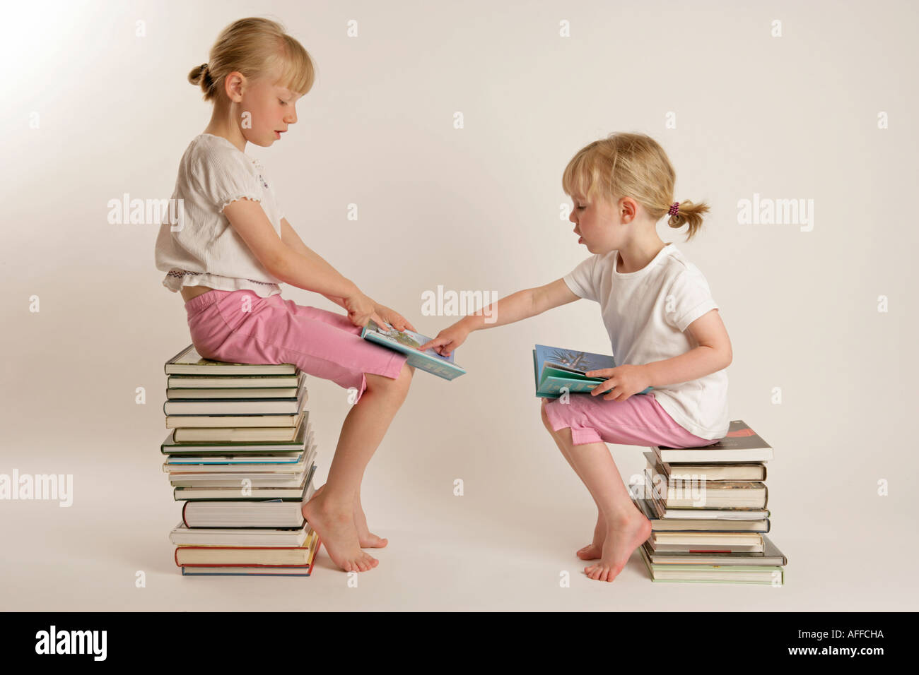 Two girls sitting on a pile of books reading together Stock Photo - Alamy