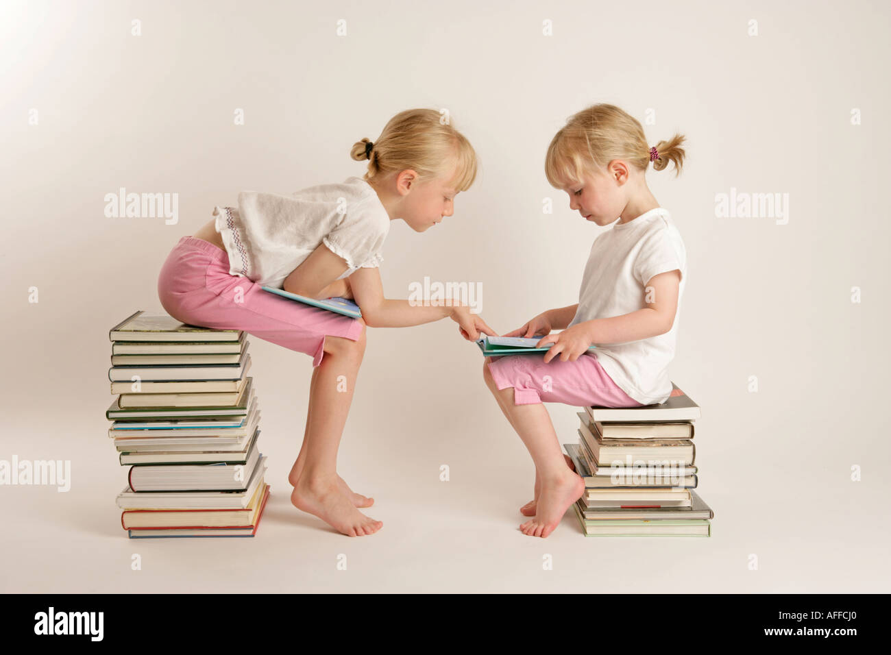 Two girls sitting on a pile of books reading together Stock Photo - Alamy