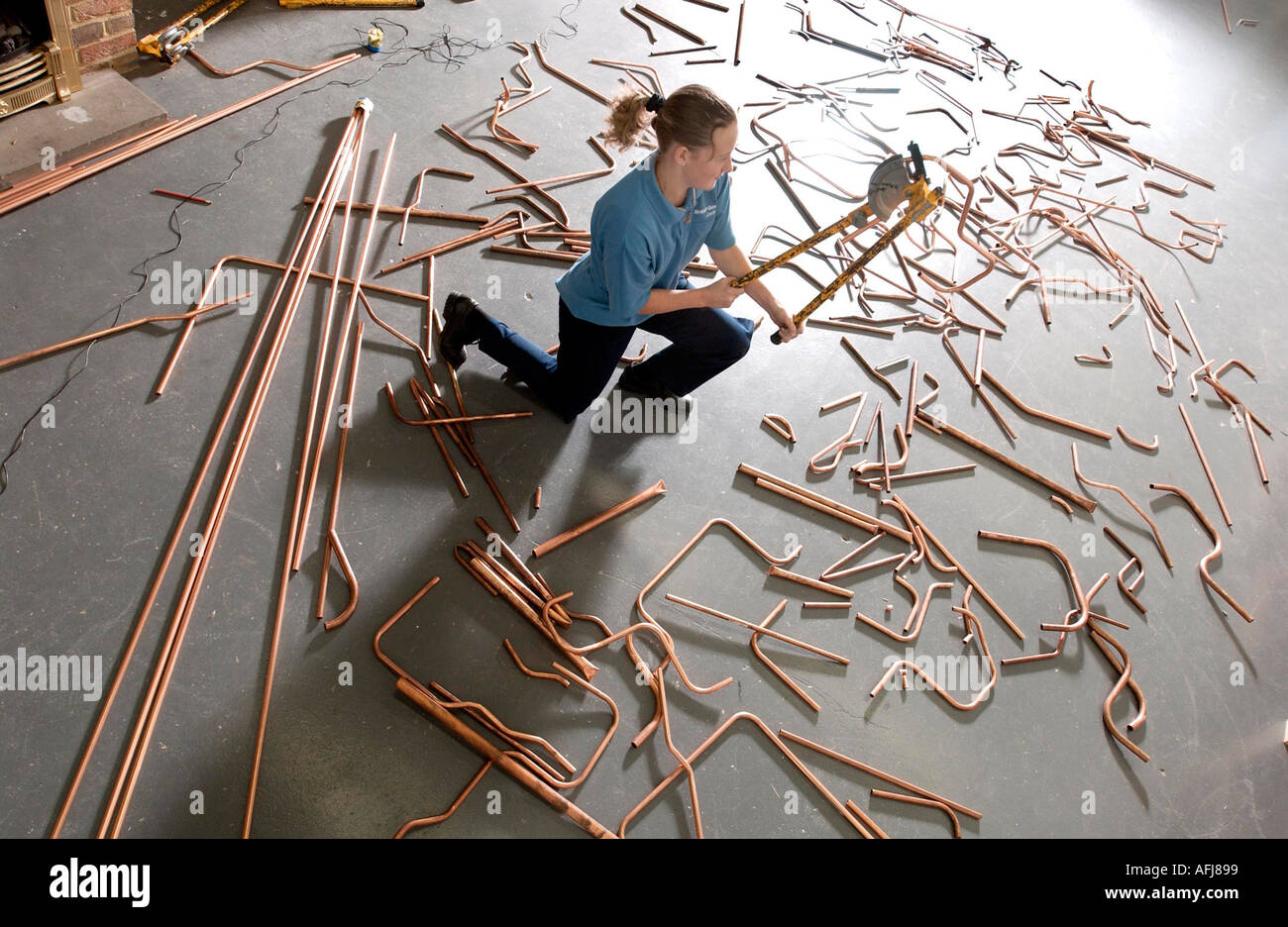 A young girl training to be a plumber with copper pipes and pipe bender ...