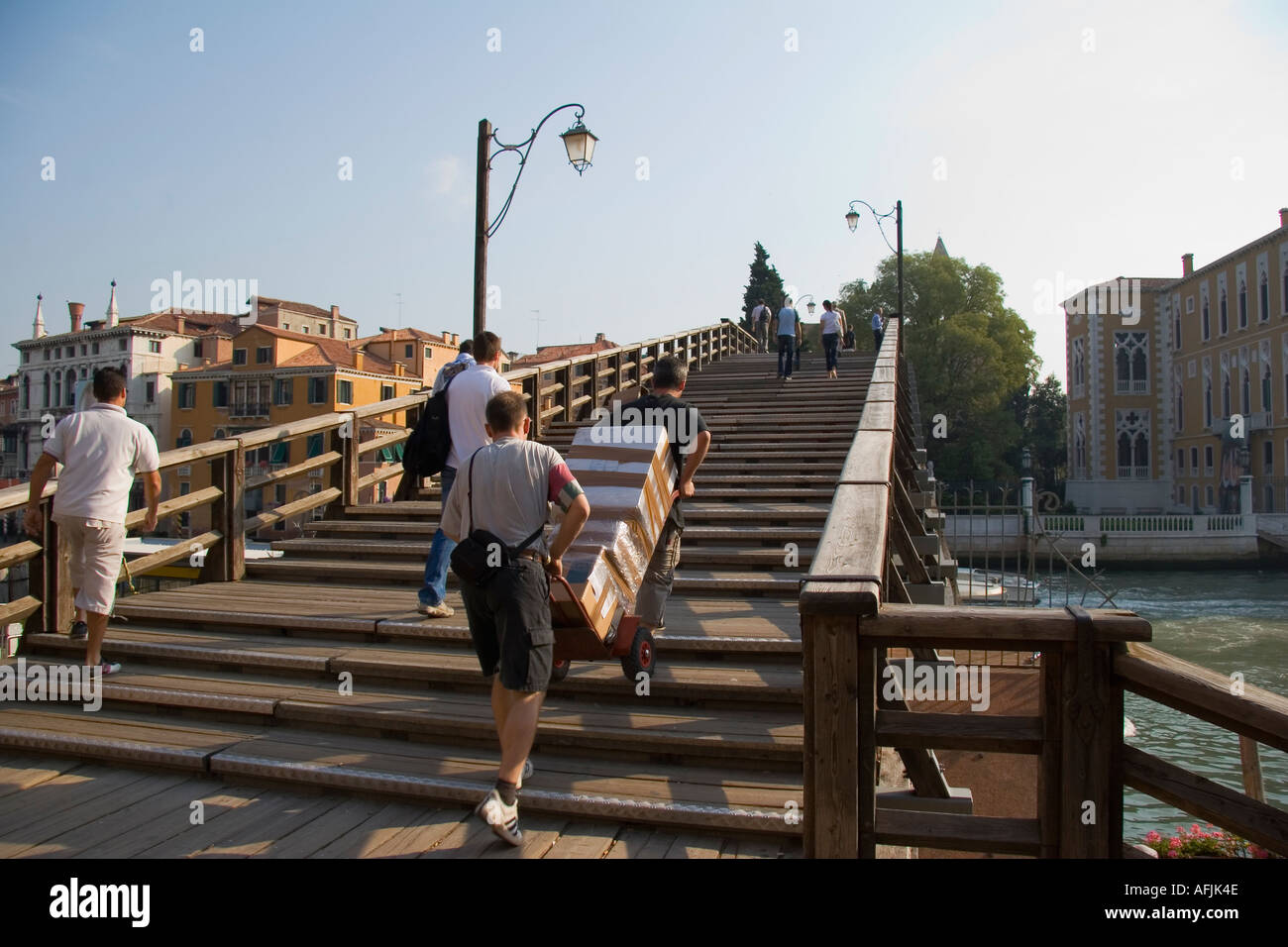 Two men carry handtruck stacked with boxes up the steps of the ...