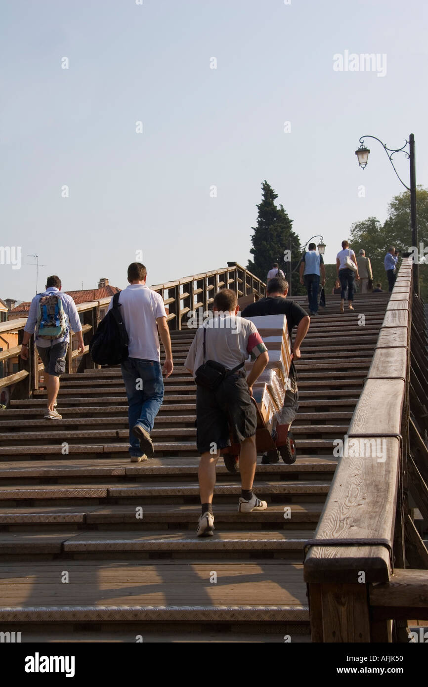 Two men carry handtruck stacked with boxes up the steps of the ...