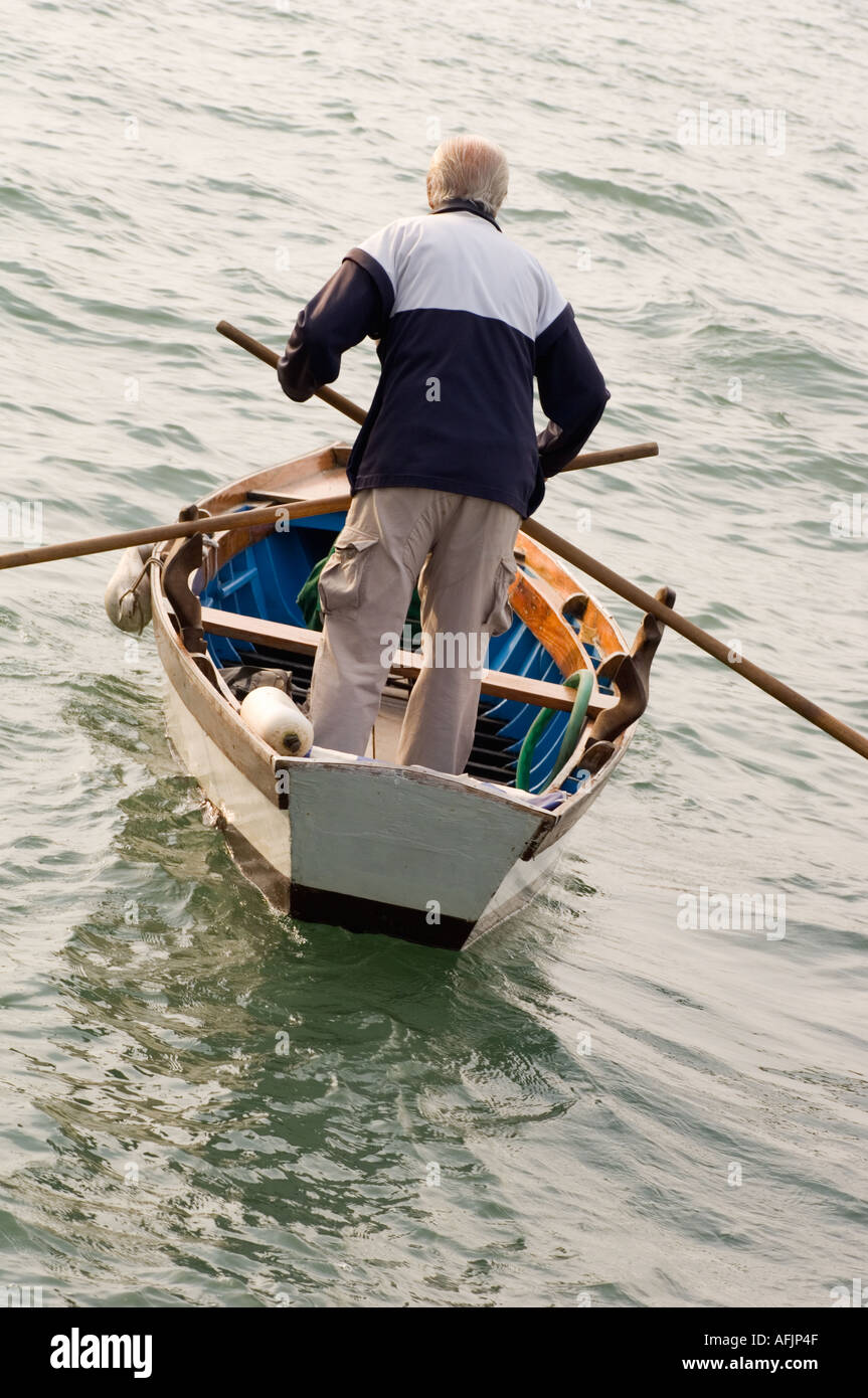 Color vertical image of an elderly main standing and rowing in a small ...