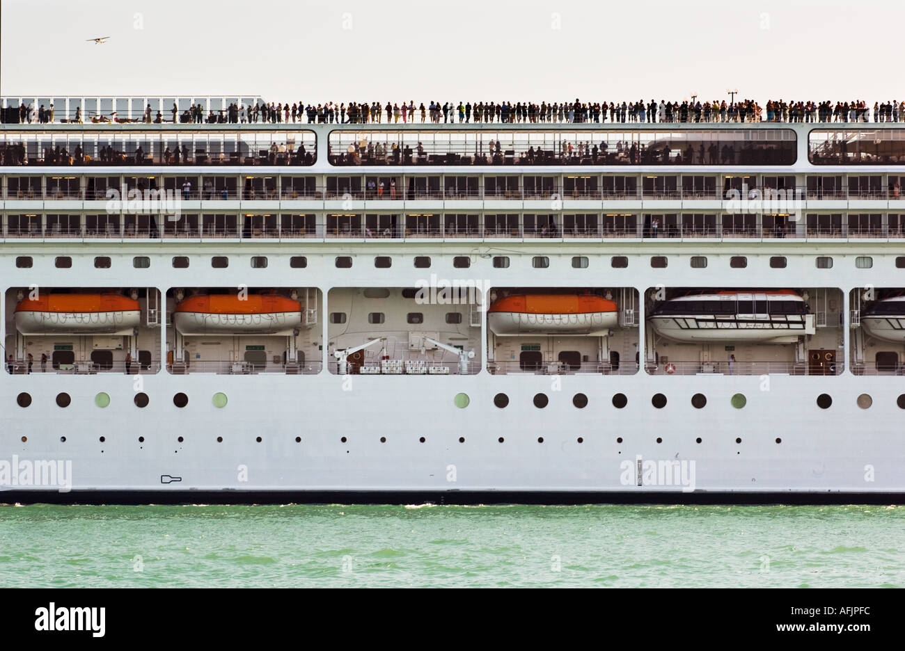 side of a large cruise ship with many people visible along the decks ...