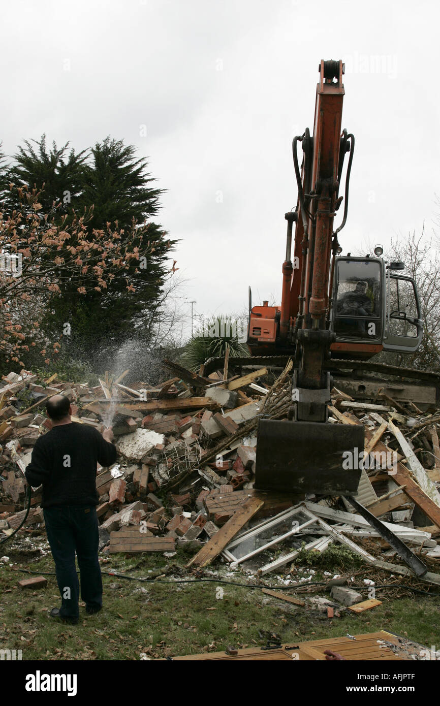 man waters rubble with water hose to damp down dust in front empty ...
