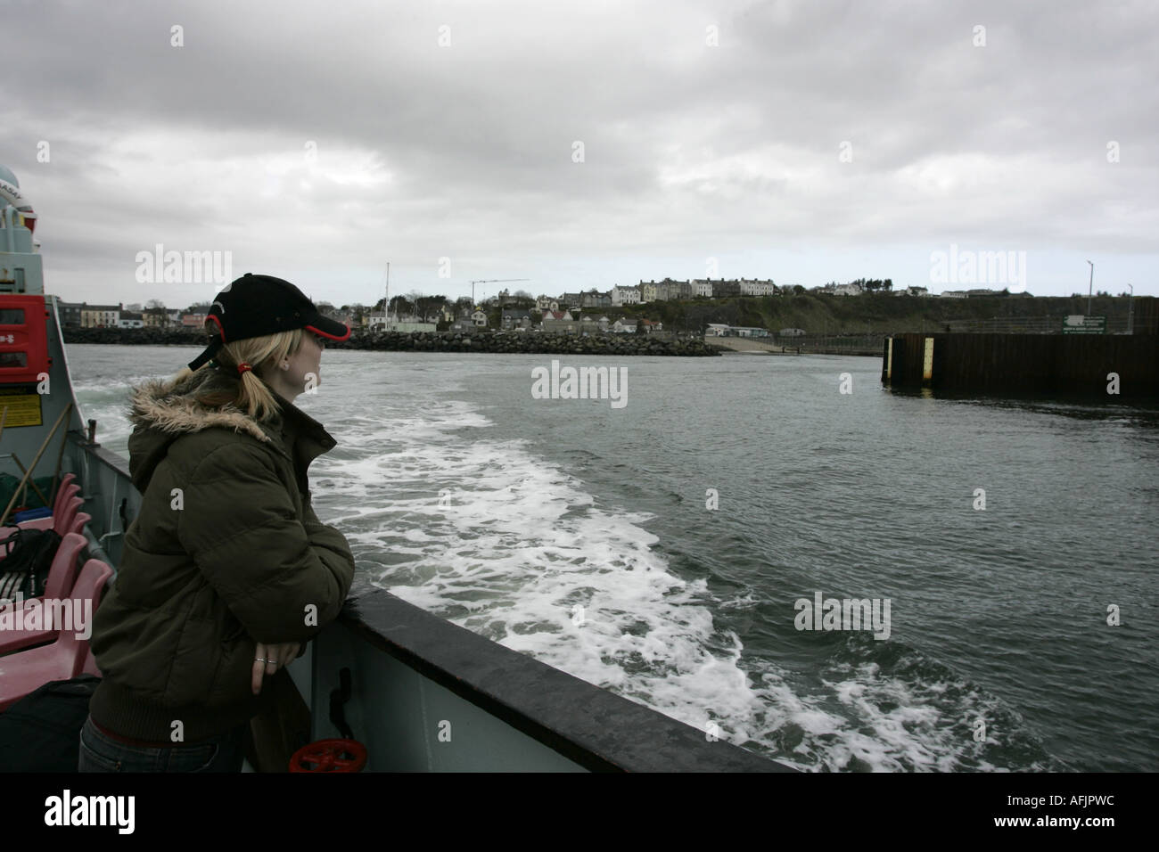 female tourist in baseball cap looks back towards Ballycastle harbour ...