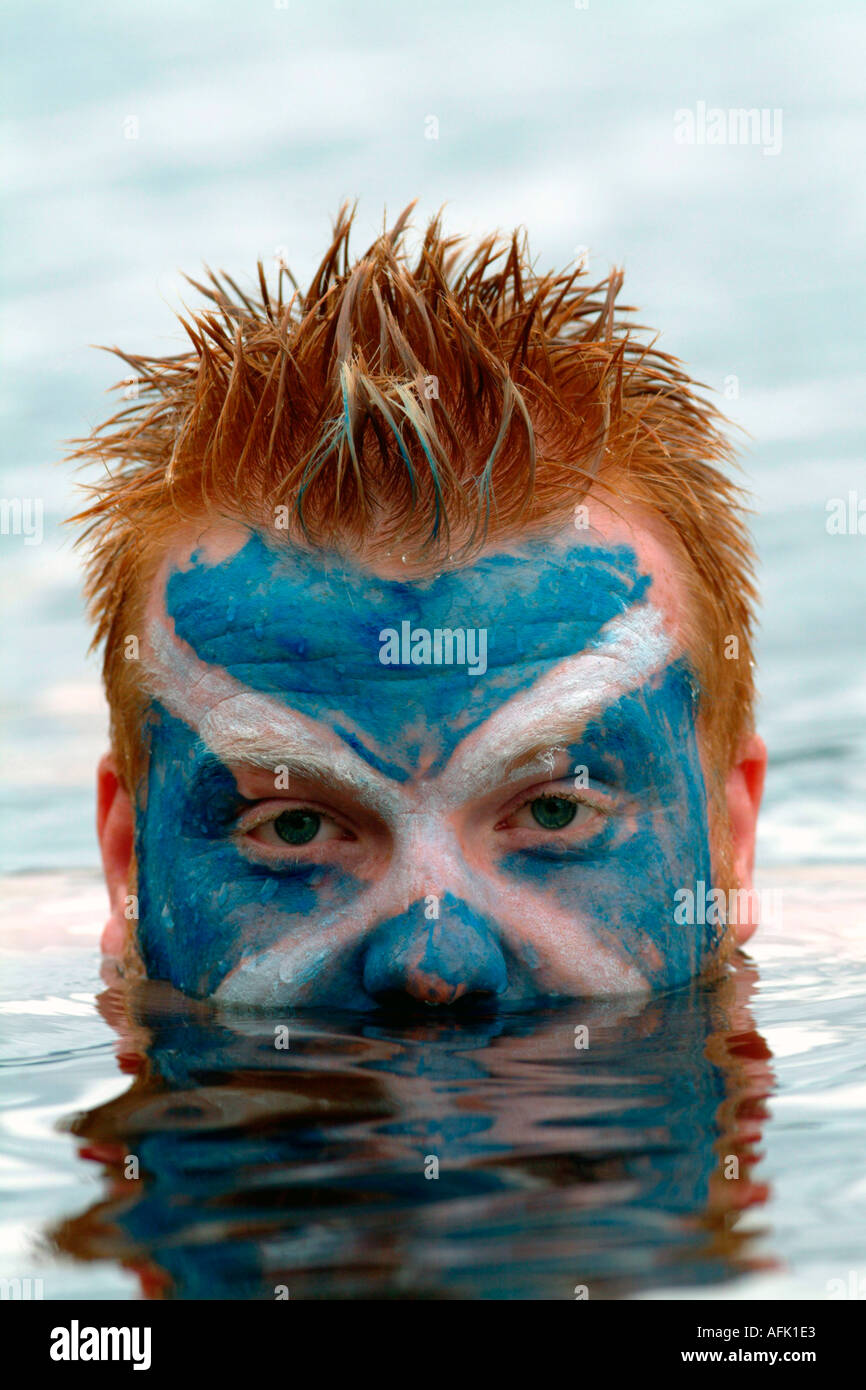 A Scotsman wearing the Scottish flag colours painted onto his face ...