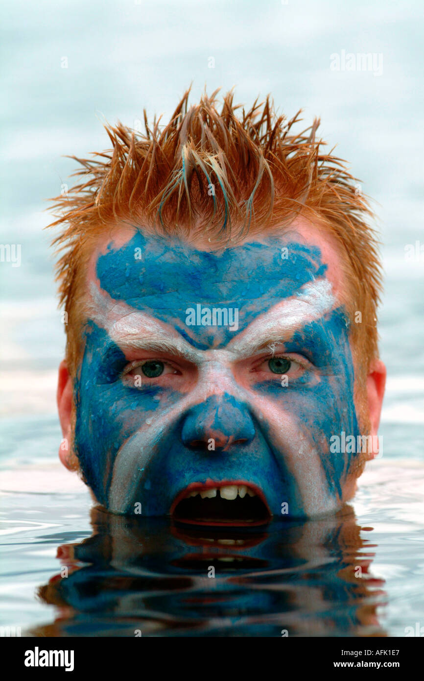 A Scotsman wearing the Scottish flag colours painted onto his face ...